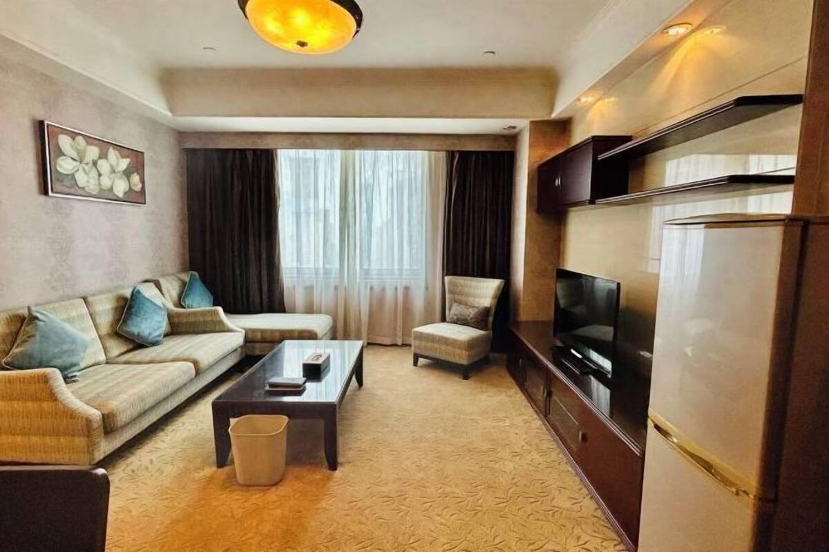 Quarto de hotel com sofá, poltrona, televisão e frigorífico.