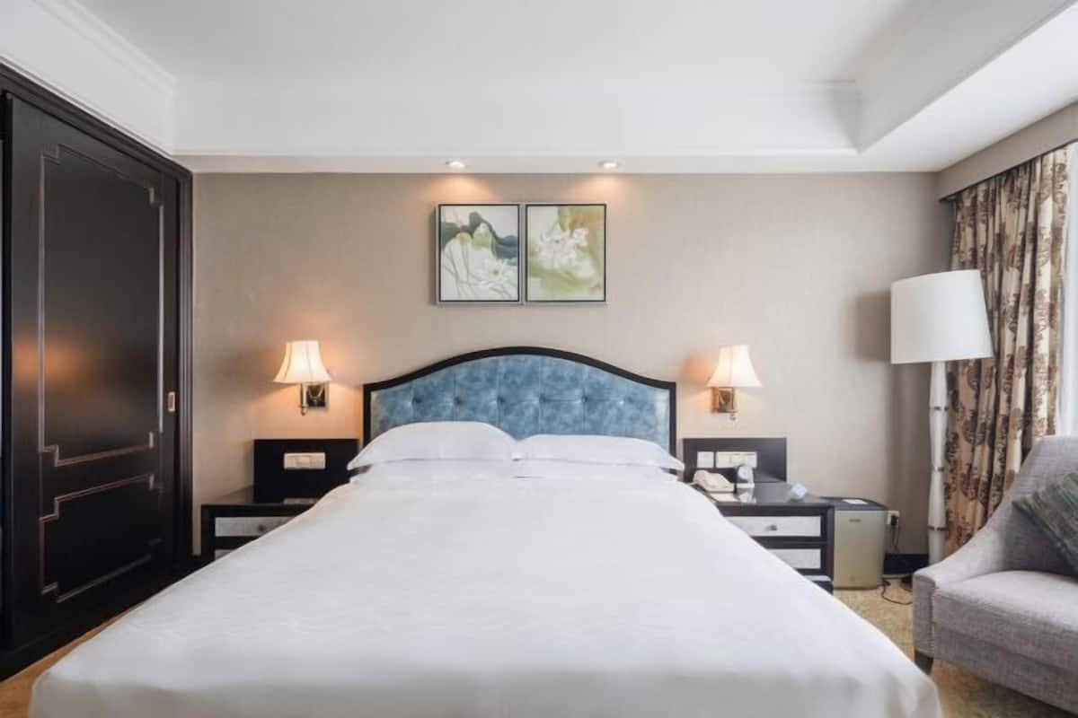 Quarto de hotel com uma cama grande, duas mesas de cabeceira com luminárias, uma cabeceira e uma cadeira.