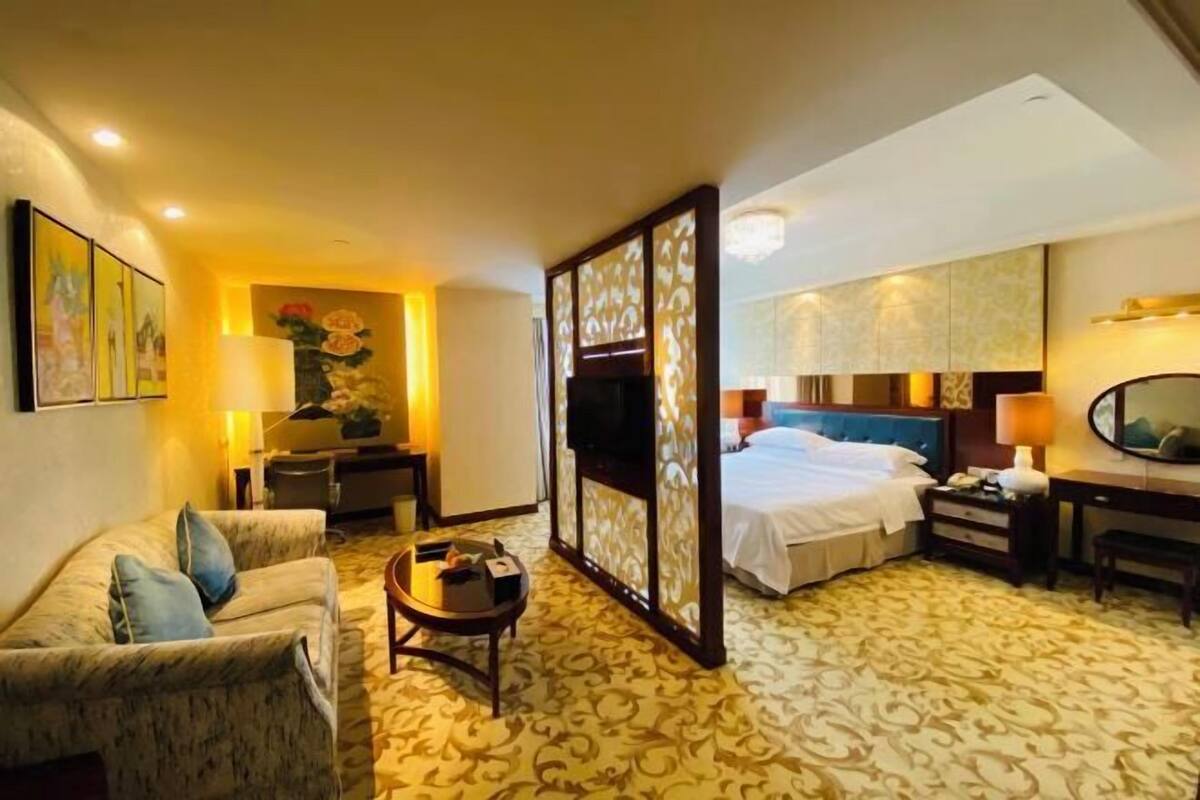 Quarto de hotel com cama, escrivaninha, cadeira, sofá e televisão.