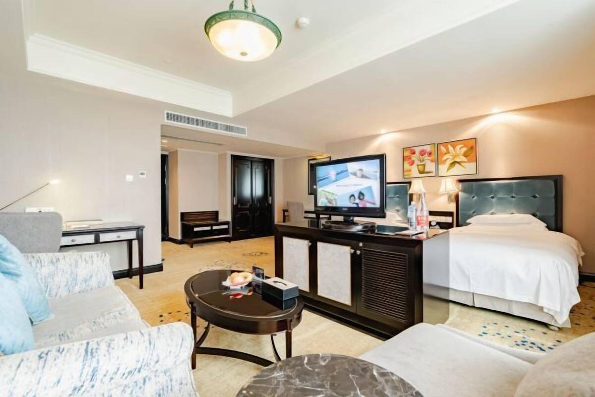 Quarto de hotel com cama, televisão, secretária e área de estar.