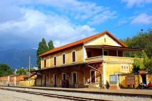 Uma estação de trem com um prédio de um andar, área de espera coberta e plataforma.