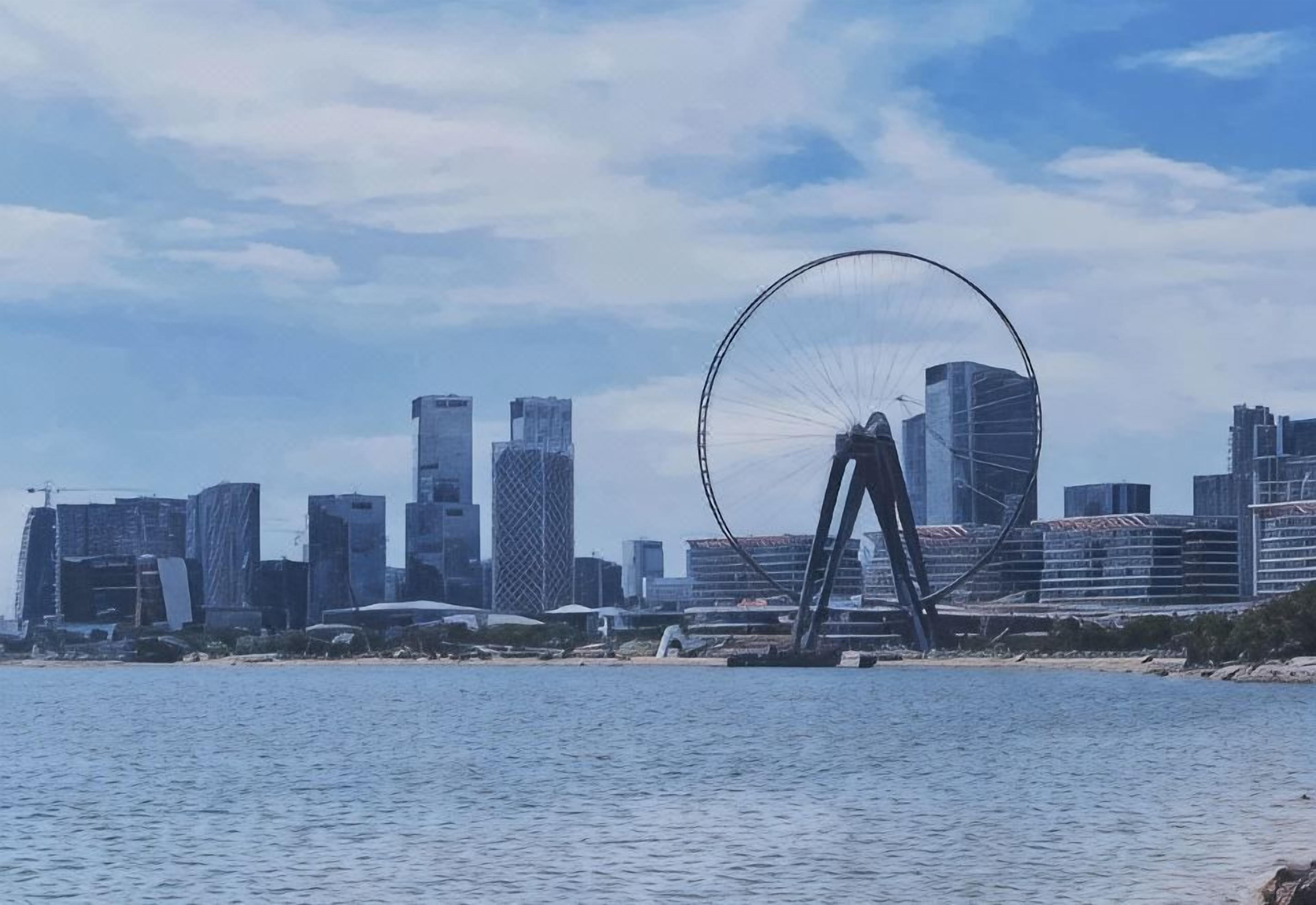 Paisagem urbana à beira-mar com edifícios modernos altos e uma grande roda gigante.