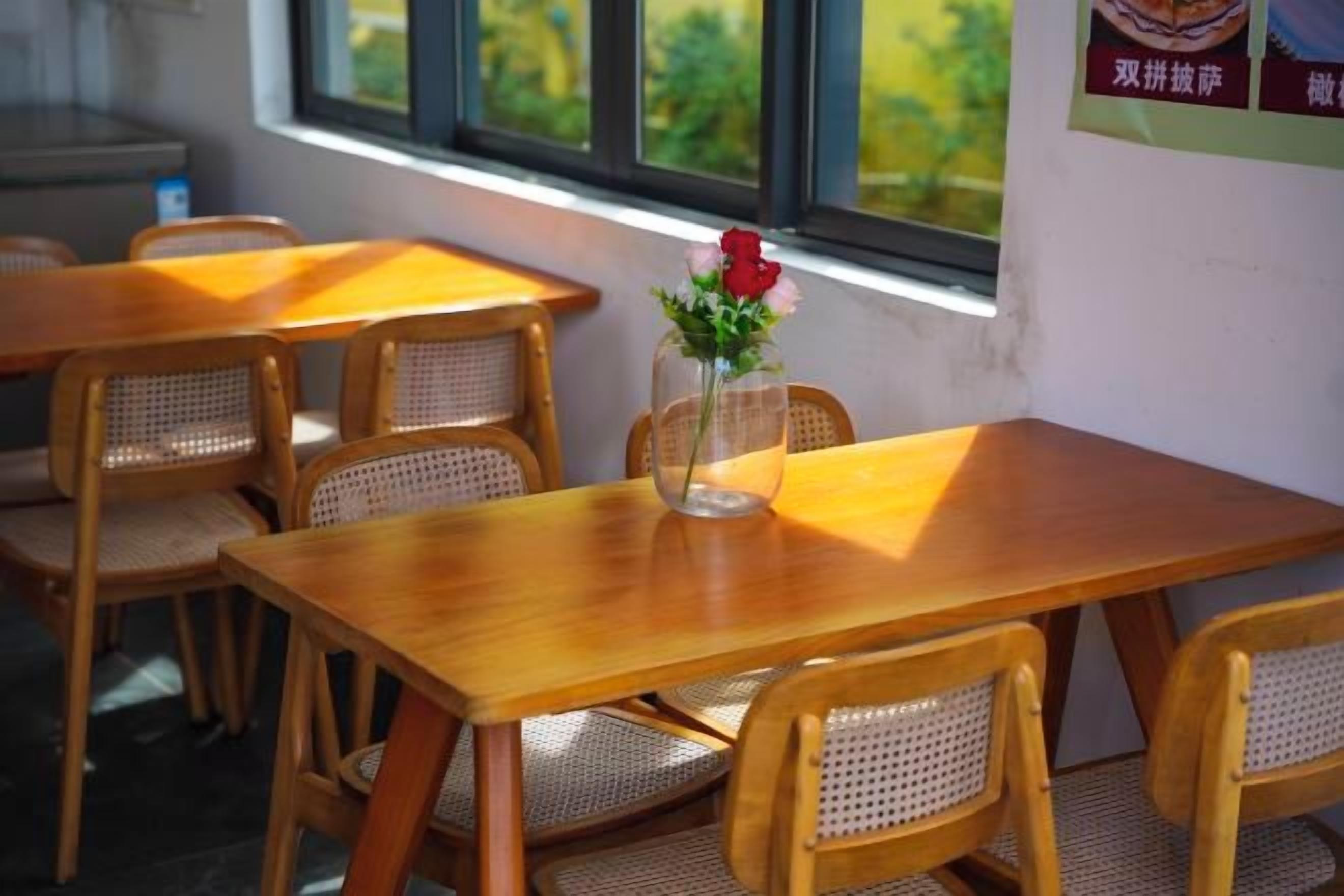 Uma mesa de madeira com um vaso de flores, rodeada por cadeiras de vime, num quarto com janela.