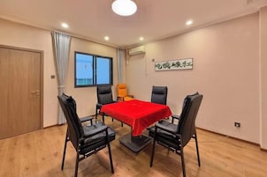 Quarto com uma mesa, quatro cadeiras, toalha de mesa vermelha, uma janela e uma porta.