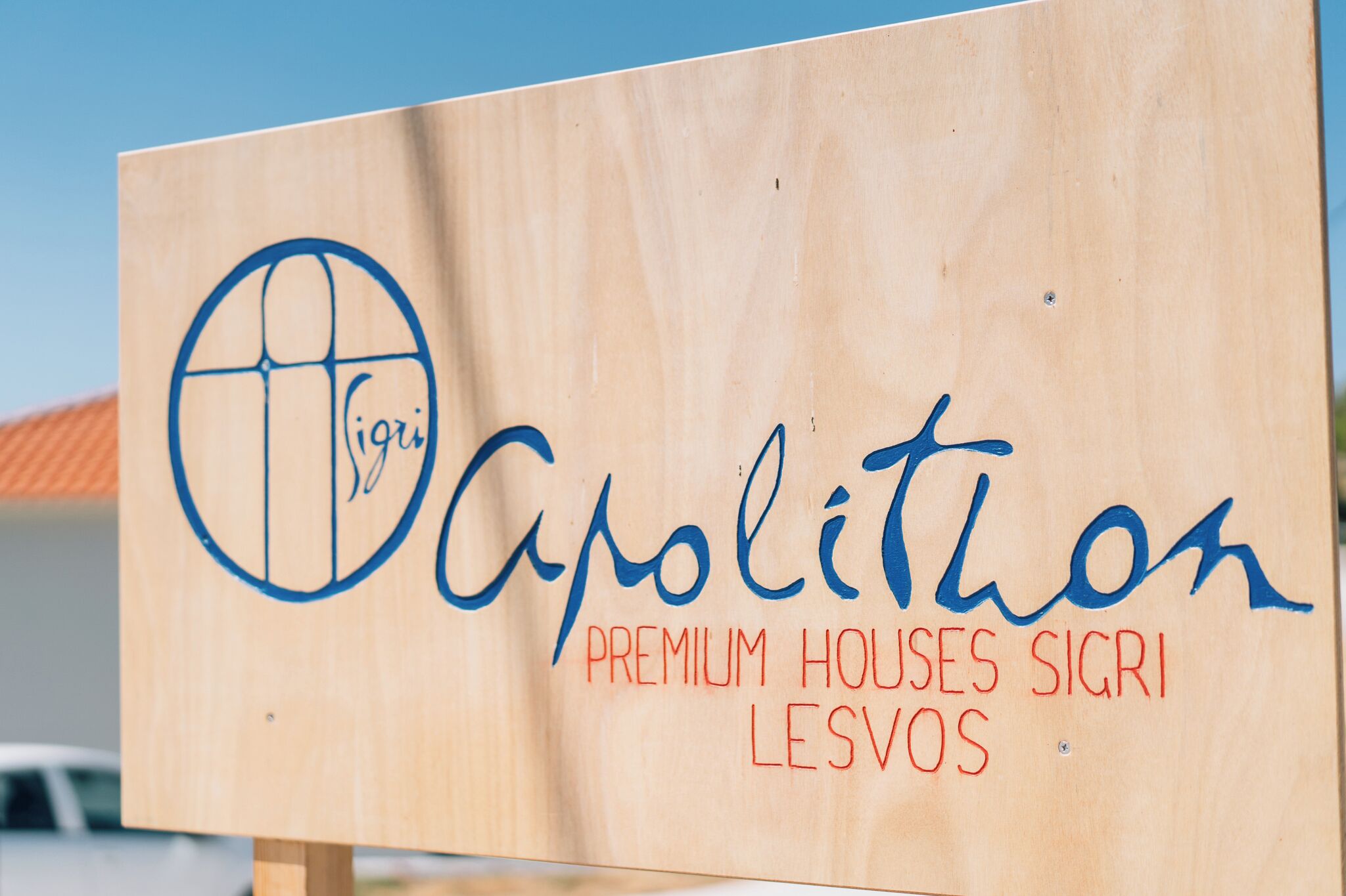Uma placa de madeira com o logotipo e o nome 'Capolition' e o texto 'PREMIUM HOUSES SIGRI LESVOS'.