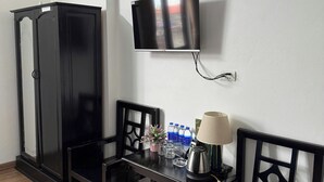 Quarto de hotel com televisão na parede, armário de madeira, mesa de jantar com cadeiras, lixeira e abajur.