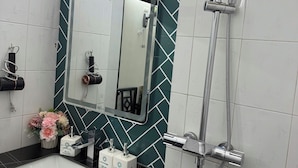 Casa de banho com lavatório branco, espelho, chuveiro e secador de cabelo.
