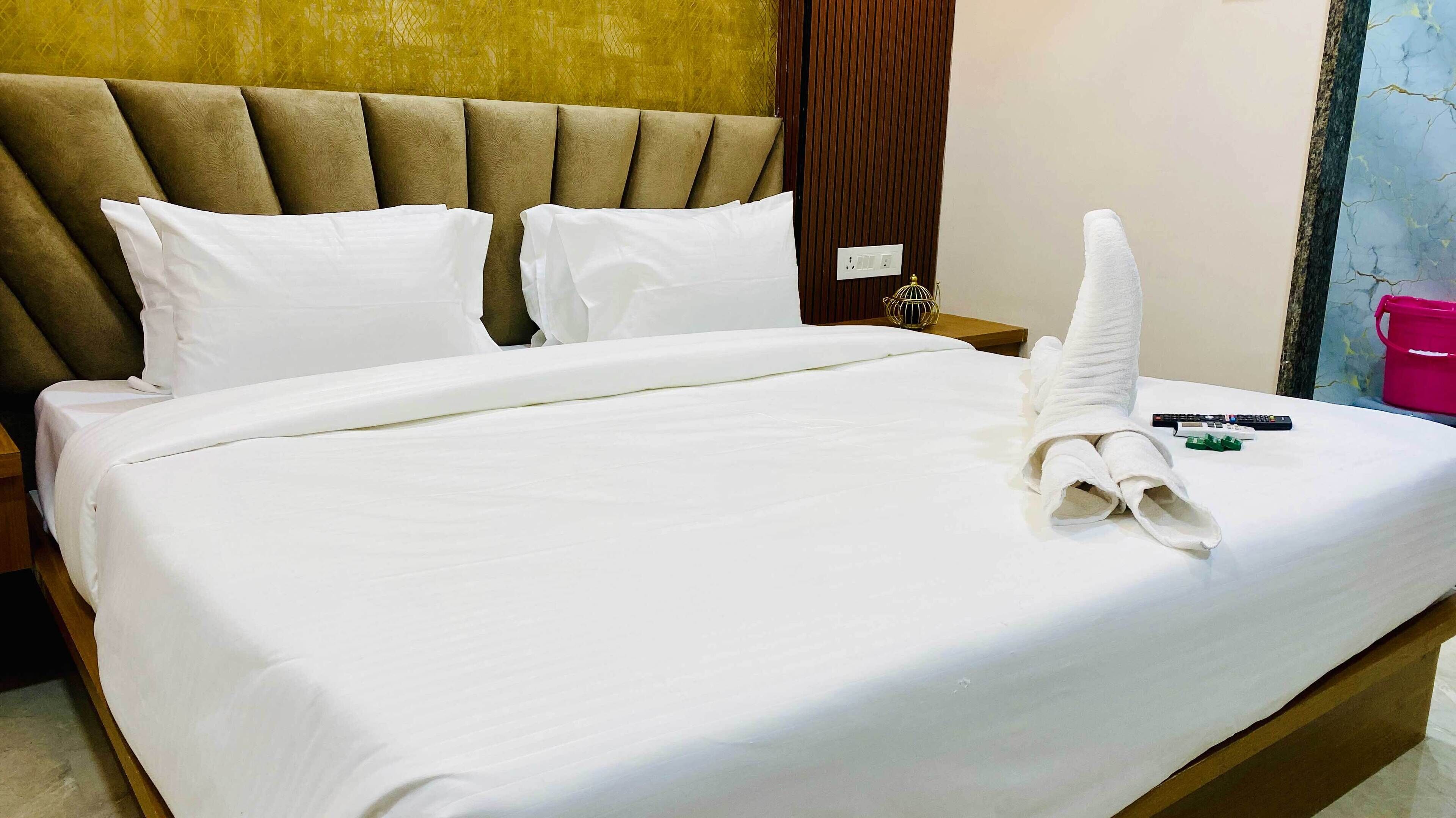 Cama bem arrumada com roupa de cama branca, toalha dobrada e controle remoto sobre a cama.
