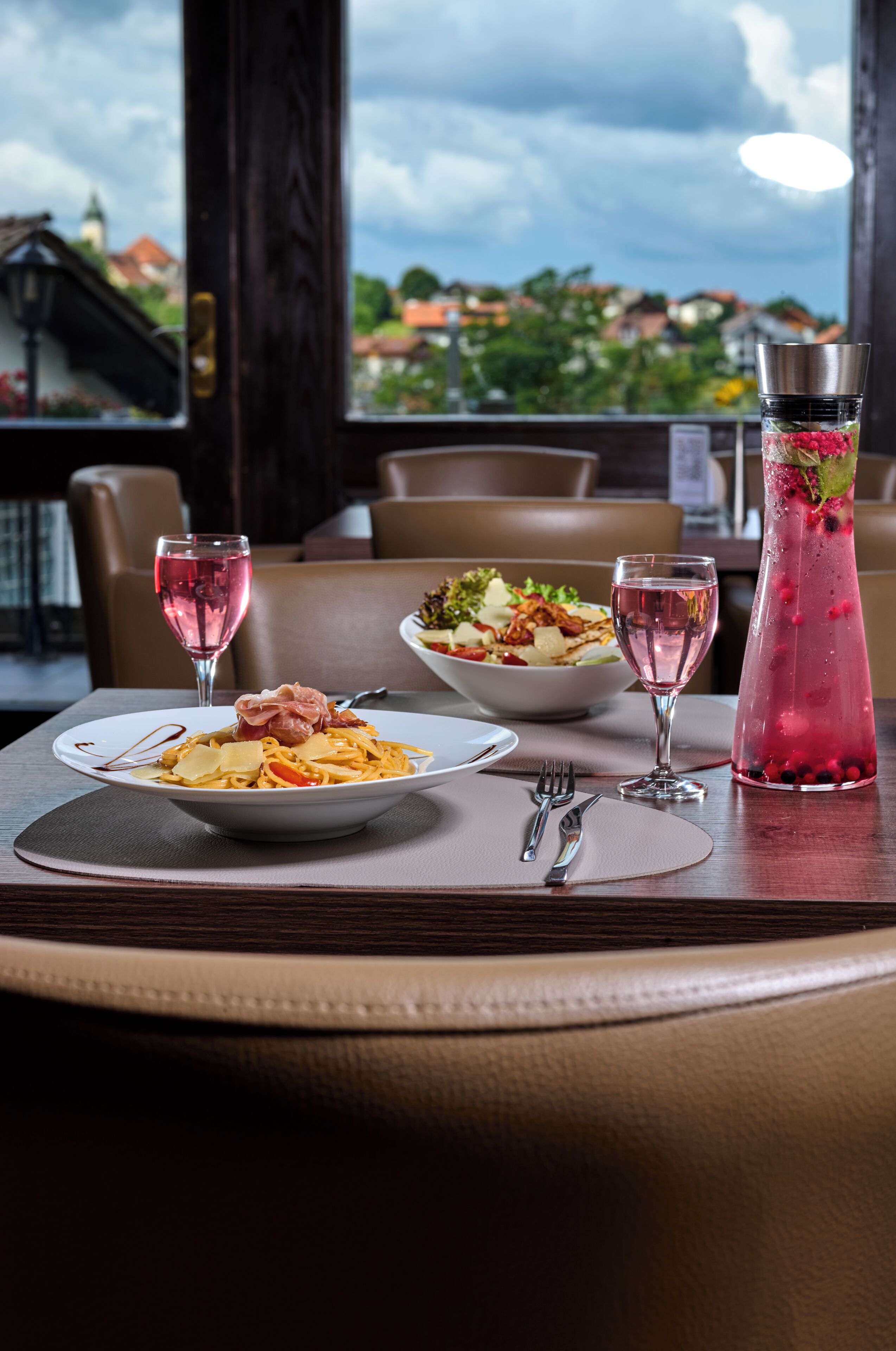 Uma mesa de jantar com dois pratos de comida, dois copos de bebida rosa e um copo alto com bebida rosa e frutas vermelhas.