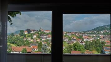 Vista da janela sobre uma cidade com casas, árvores e uma colina com uma igreja.