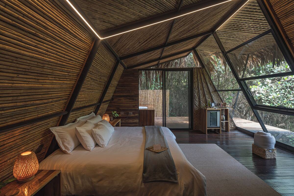 Quarto moderno com telhado triangular, uma cama grande, luminárias de cabeceira e vista para o exterior.