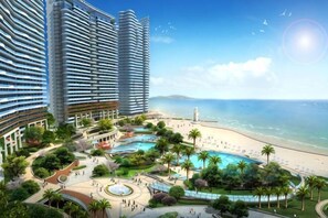 Um resort costeiro com edifícios altos, uma praia, área de piscina e um calçadão.