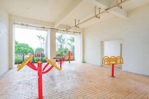 Espaço coberto para brincar, com área ampla, equipamentos de exercício e vista para o verde lá fora.