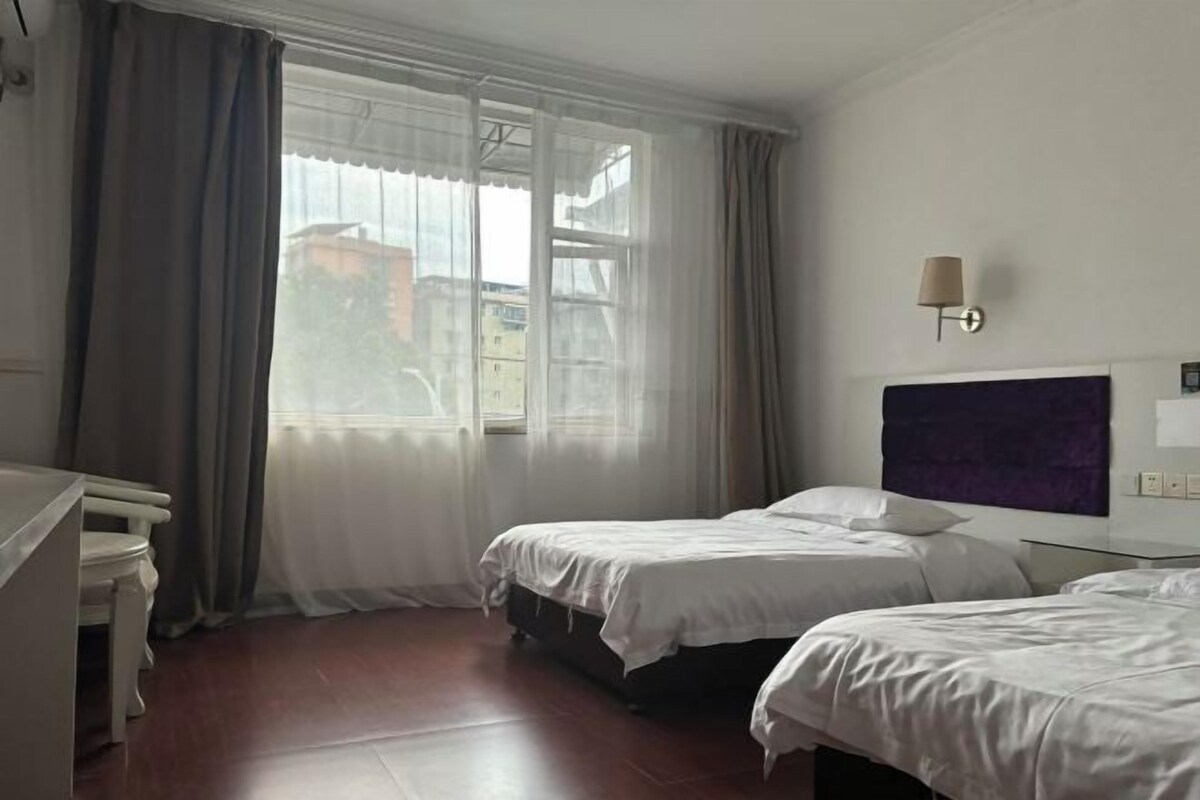 Quarto de hotel com duas camas, uma escrivaninha e uma janela com cortinas.