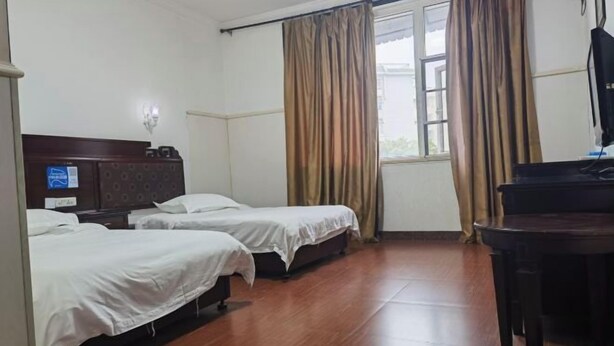 Quarto de hotel com duas camas de solteiro, piso de madeira, escrivaninha com cadeira e janela com cortinas.