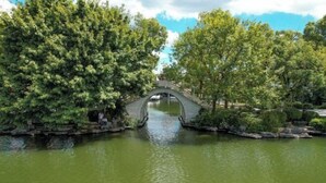 Uma ponte de pedra sobre águas calmas, cercada por vegetação exuberante.