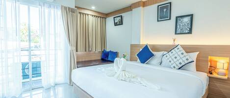 Quarto de hotel com uma cama grande, uma mesa de cabeceira com abajur, uma janela com cortinas e um painel de parede com quadros.