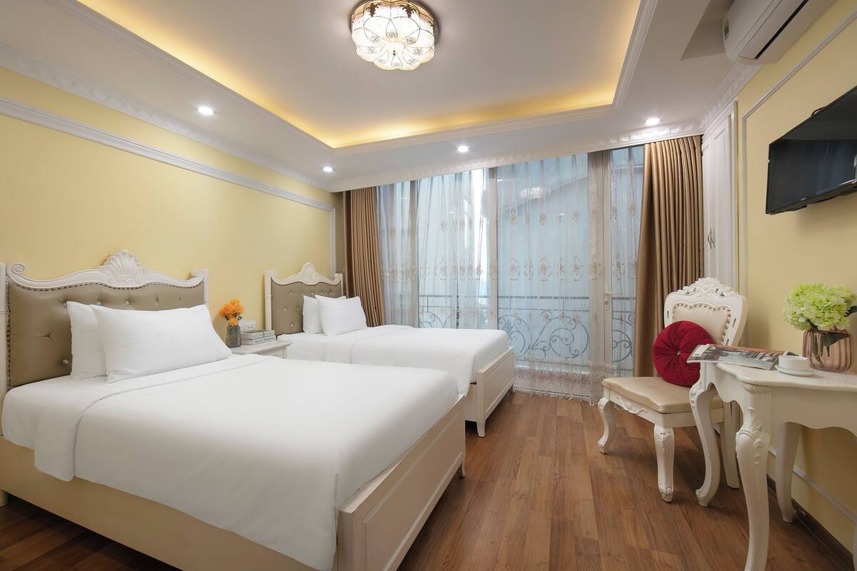 Quarto de hotel com duas camas, uma escrivaninha, uma cadeira e uma televisão.