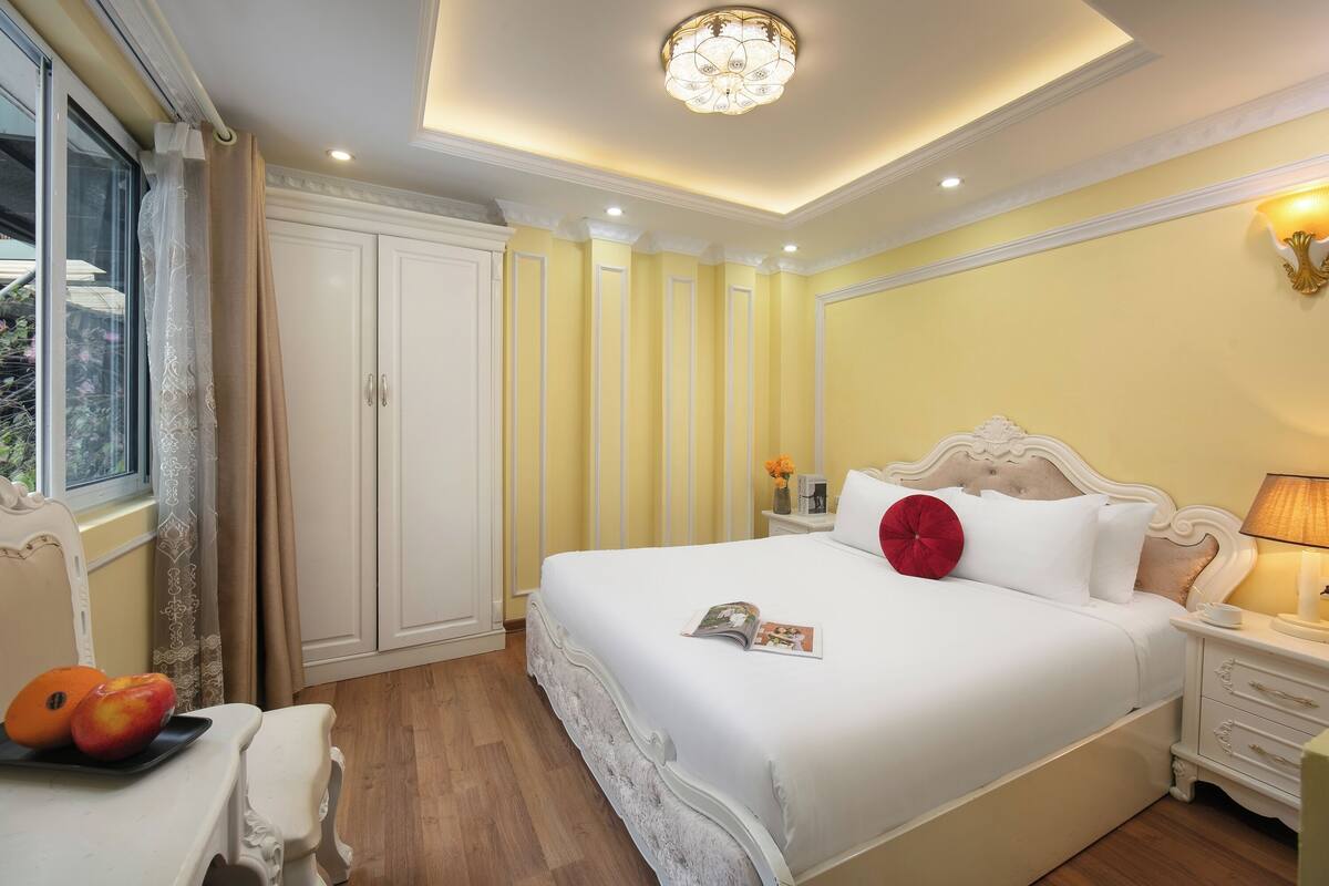 Quarto de hotel bem arrumado, com uma cama grande, mesas de cabeceira e uma janela com cortinas.