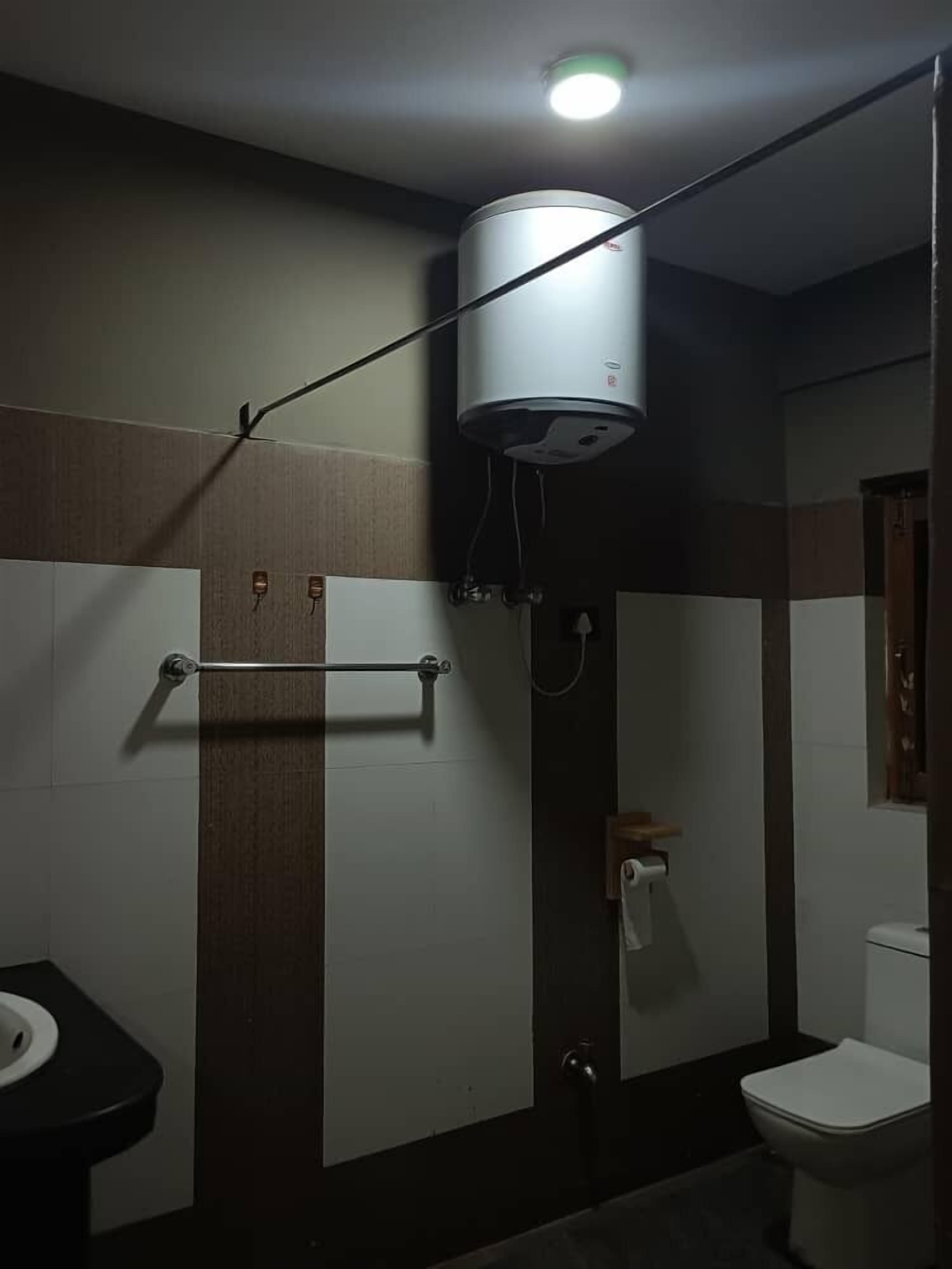 Um banheiro com vaso sanitário, pia, porta-toalhas, chuveiro e unidade de ar condicionado no teto.