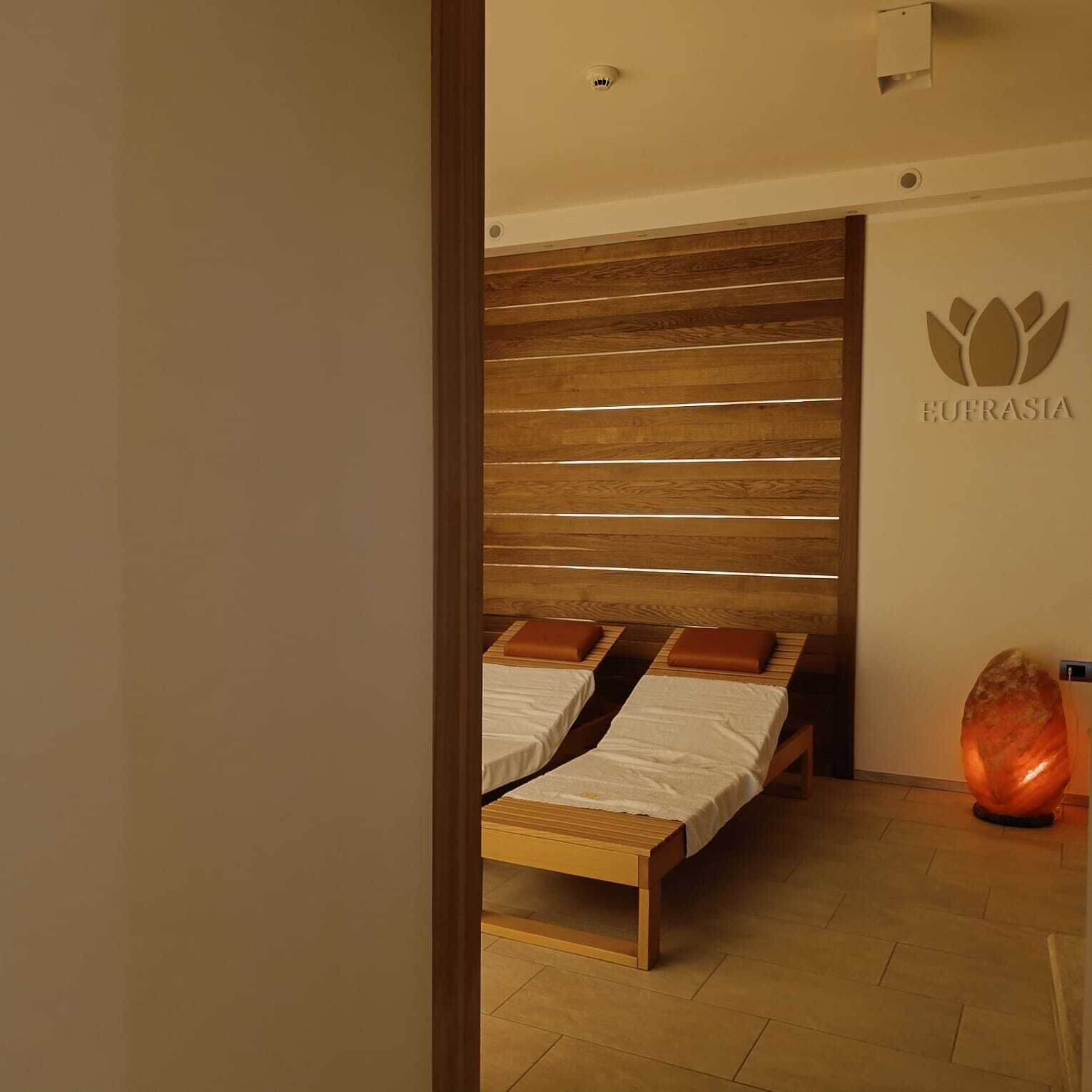 Um espaço de spa com parede de ripas de madeira, duas camas com roupa de cama branca e uma escultura de pedra aquecida.