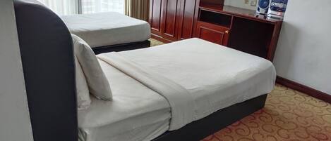 Quarto de hotel com duas camas, uma mesa de trabalho com caixas de som e vista da cidade por grandes janelas.