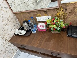 Uma escrivaninha de madeira com uma chaleira, garrafas de água, um estojo de lenços de papel, um telefone e uma planta decorativa.