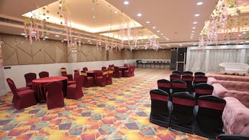 Uma sala de banquetes com mesas redondas e cadeiras, piso estampado e decorações florais pendentes.