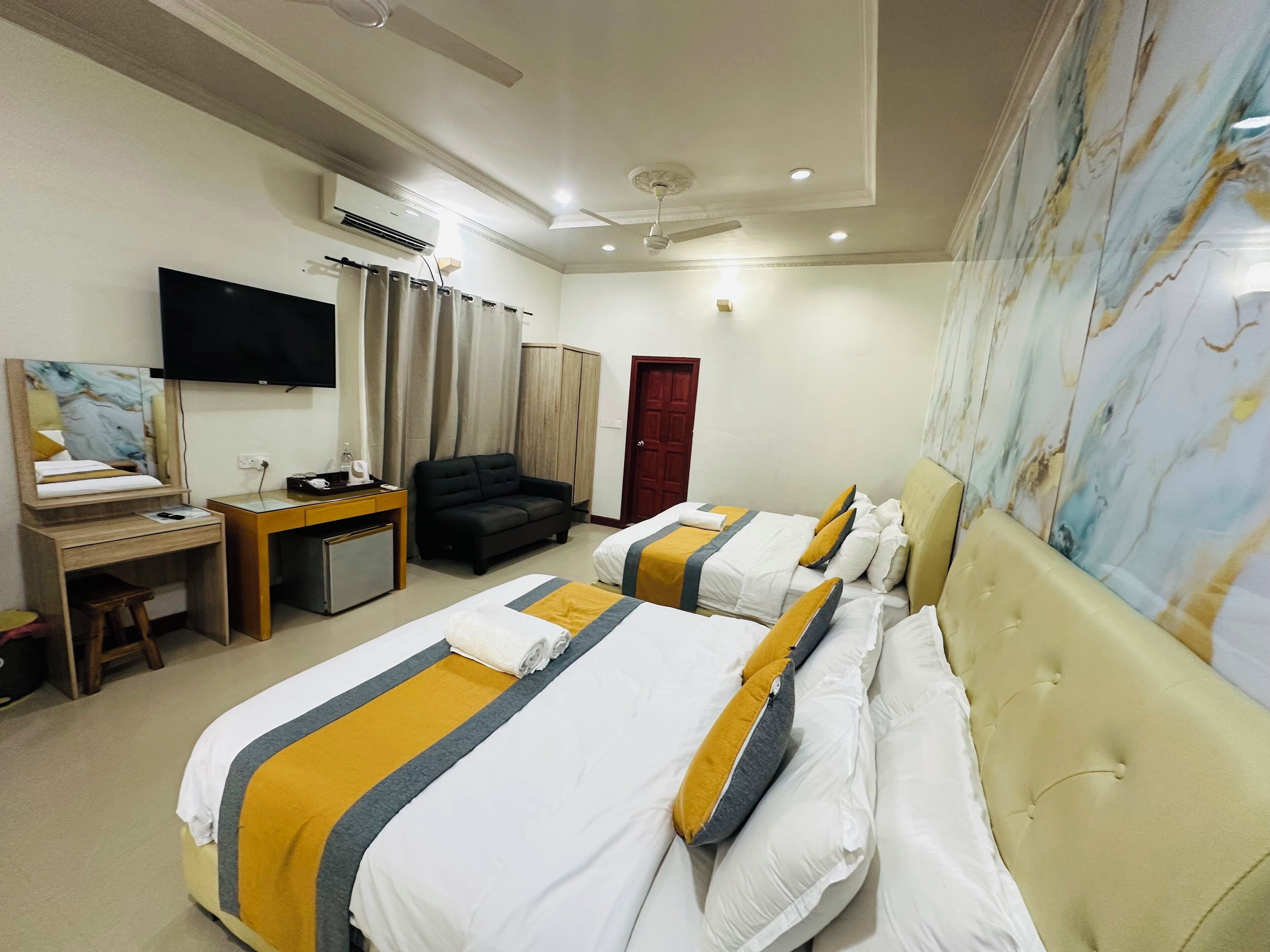Quarto de hotel com duas camas, uma escrivaninha, uma cadeira, uma televisão e um guarda-roupa.