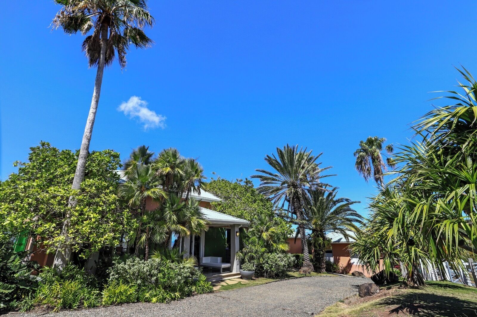 Um resort tropical com palmeiras, uma entrada de cascalho e um edifício com telhado branco.