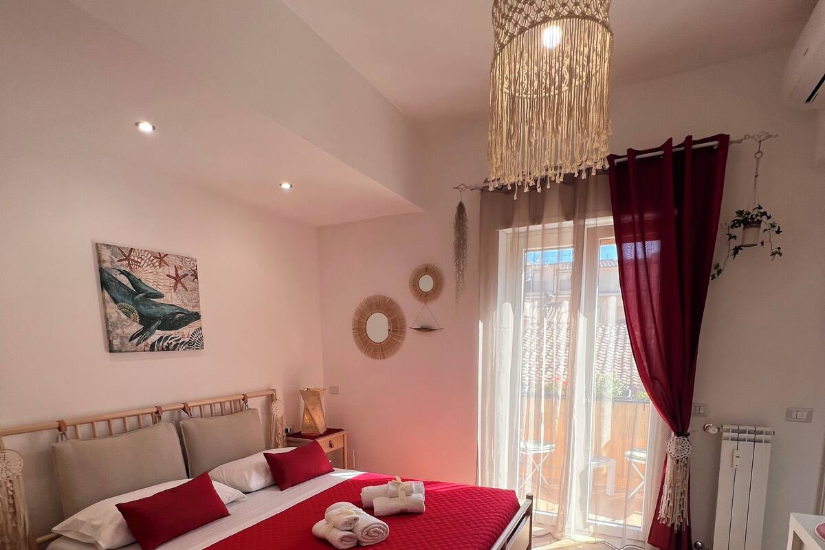 Quarto com cama grande, luminária de cristal, janela com cortinas e radiador.