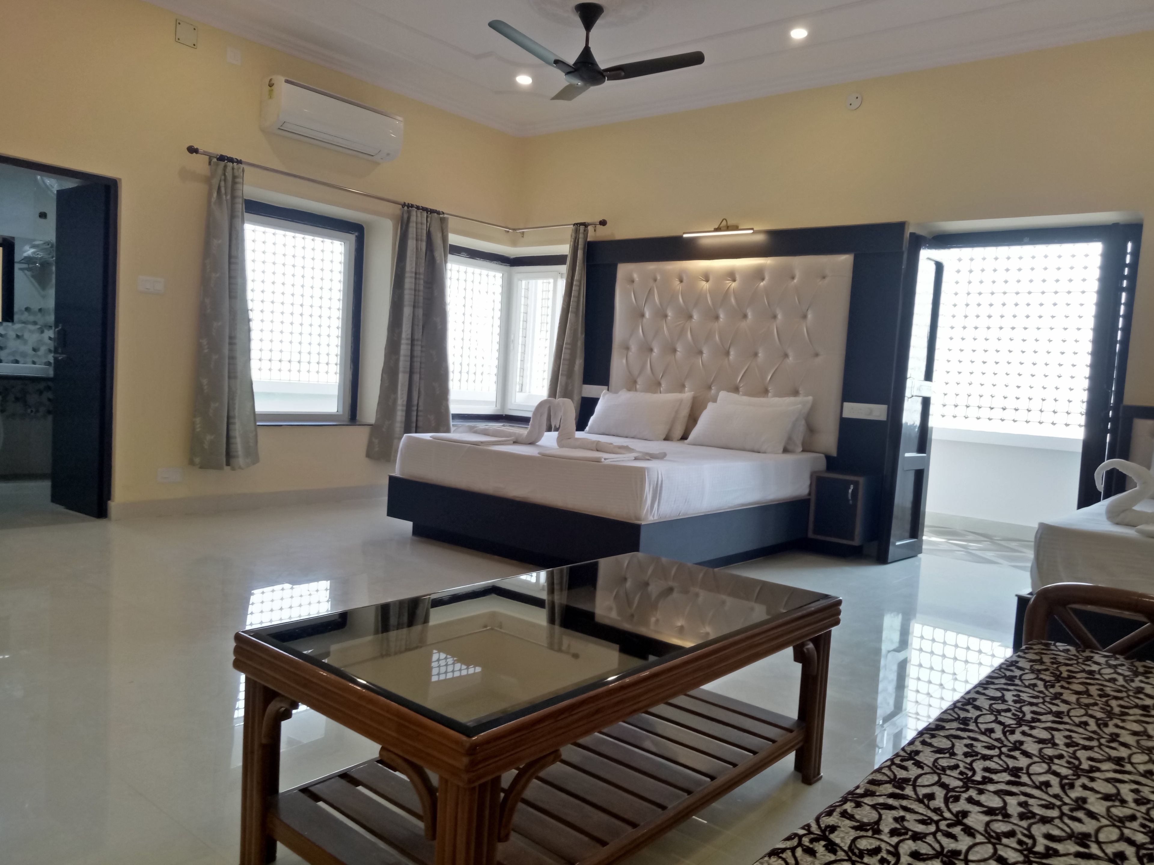 Quarto de hotel com cama, mesa de vidro e vista para o exterior.