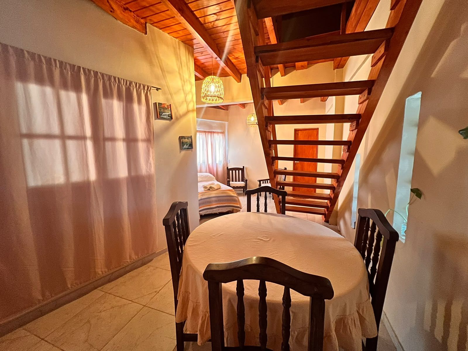 Quarto com escada de madeira, cama com cobertor listrado e mesa com cadeiras.