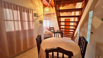Quarto com escada de madeira, cama com cobertor listrado e mesa com cadeiras.