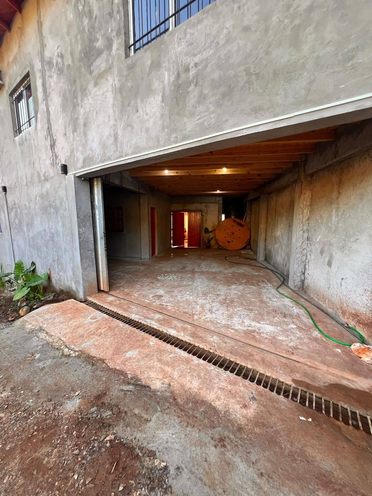 Um edifício inacabado com fachada de concreto, teto de madeira e porta de metal.