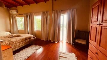 Quarto com cama, cadeira, armário de madeira e janela com cortinas.
