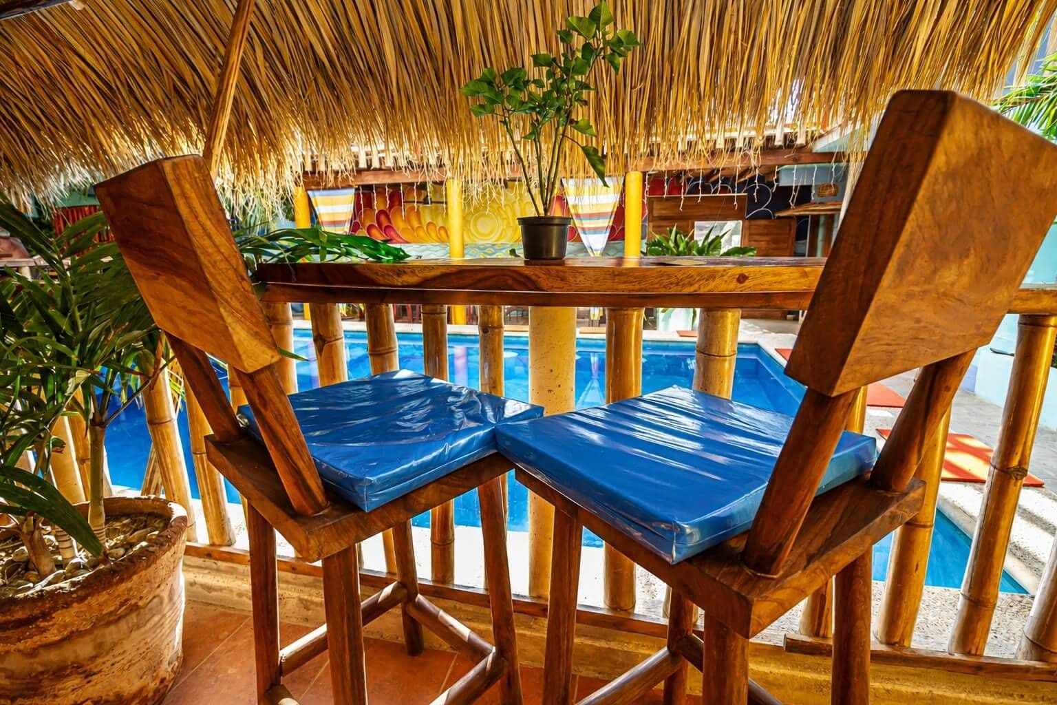 Um deck de madeira com duas cadeiras e uma mesa, com vista para uma área de piscina.
