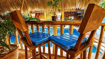 Um deck de madeira com duas cadeiras e uma mesa, com vista para uma área de piscina.