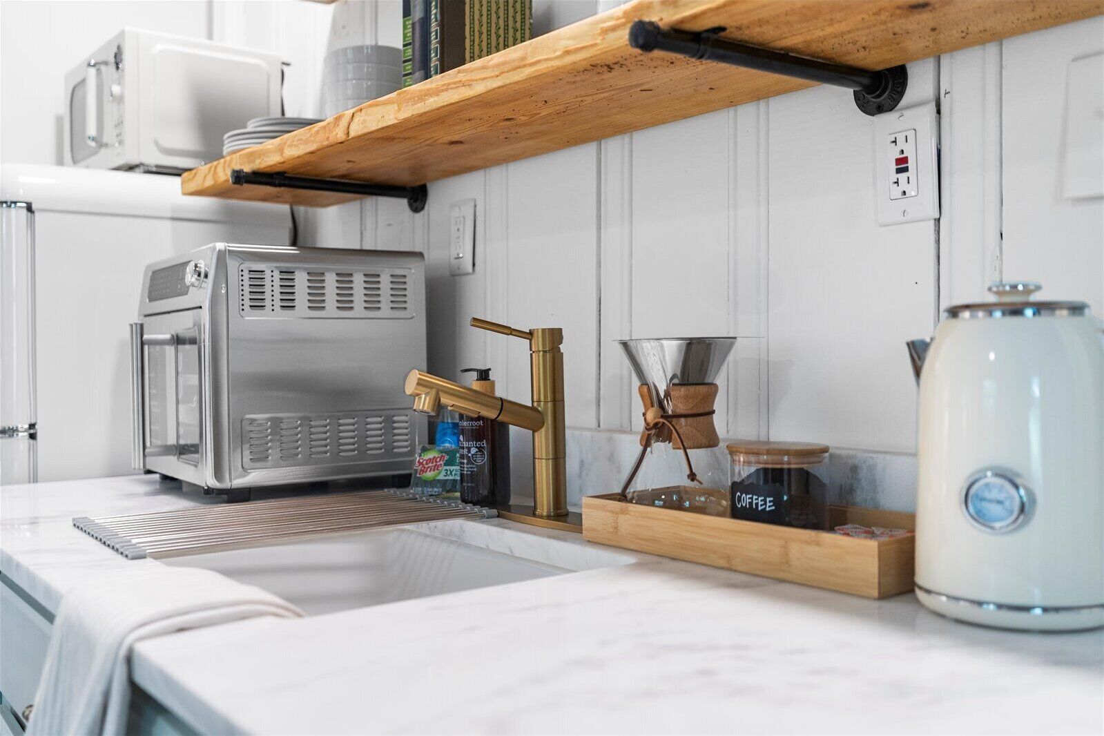 Uma cozinha com máquina de espresso embutida, moedor de café e chaleira no balcão.