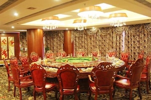 Uma sala de jantar formal com uma mesa redonda, cadeiras estofadas em vermelho e decorações de parede elaboradas.
