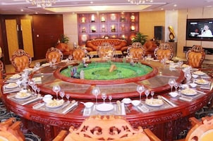 Mesa de jantar redonda com cadeiras, um elemento decorativo central, e uma tela de televisão ao fundo.