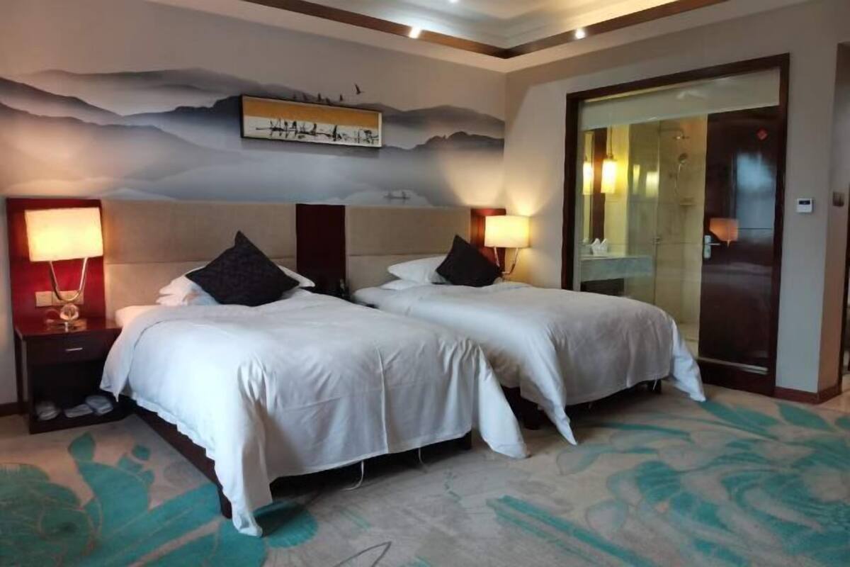 Quarto de hotel com duas camas, um espelho grande, um quadro na parede e piso coberto por carpete.