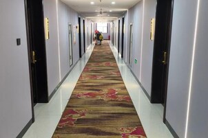 Corredor de hotel com portas em ambos os lados, carpete estampado e uma pessoa caminhando ao longe.