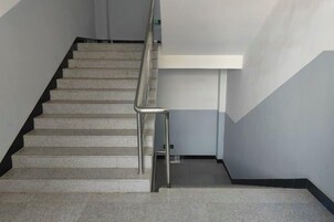 Uma escadaria com corrimão de metal, que leva a um patamar com parede branca e rodapé preto.
