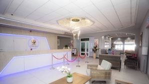 Uma área de recepção de hotel com design moderno, apresentando um balcão de atendimento, área de estar e um teto decorativo.