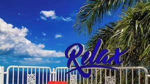 Duas cadeiras de balanço vermelhas em frente a uma cerca de metal branca com uma placa que diz 'Relax'.