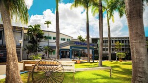 Pátio de hotel com palmeiras, um banco de madeira e uma grande roda de madeira.