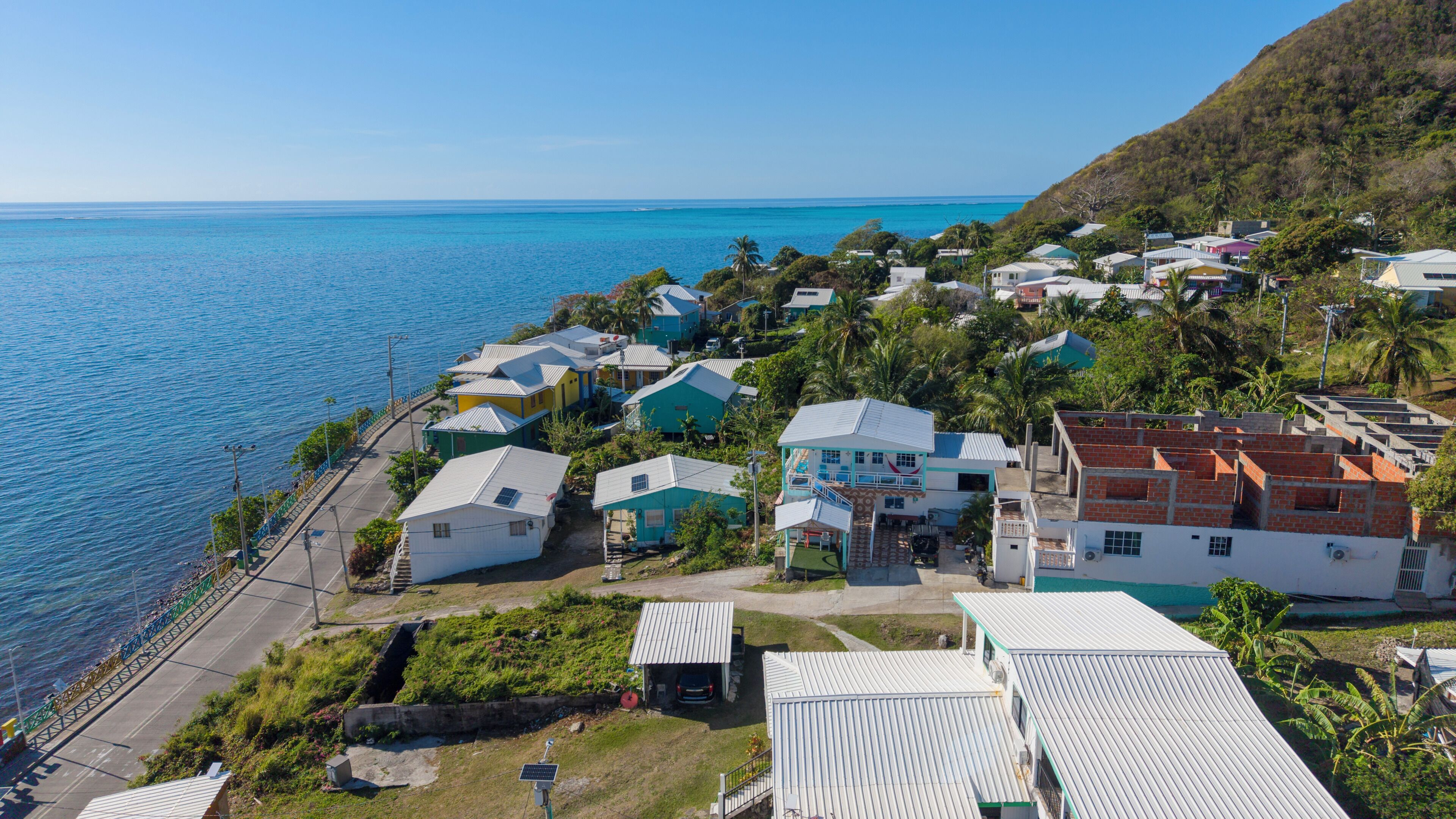 Uma vila costeira com casas, uma estrada e vista para o mar.