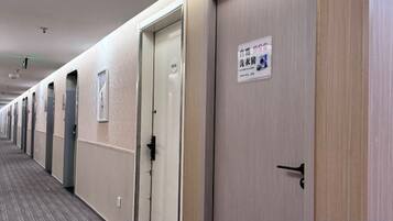 Corredor de hotel com portas, algumas com placas indicativas, e piso coberto por carpete.