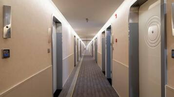 Corredor de hotel com portas em ambos os lados, piso coberto de carpete e luminária no teto.